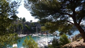 Uma marina com barcos atracados, rodeada por árvores e terreno rochoso.