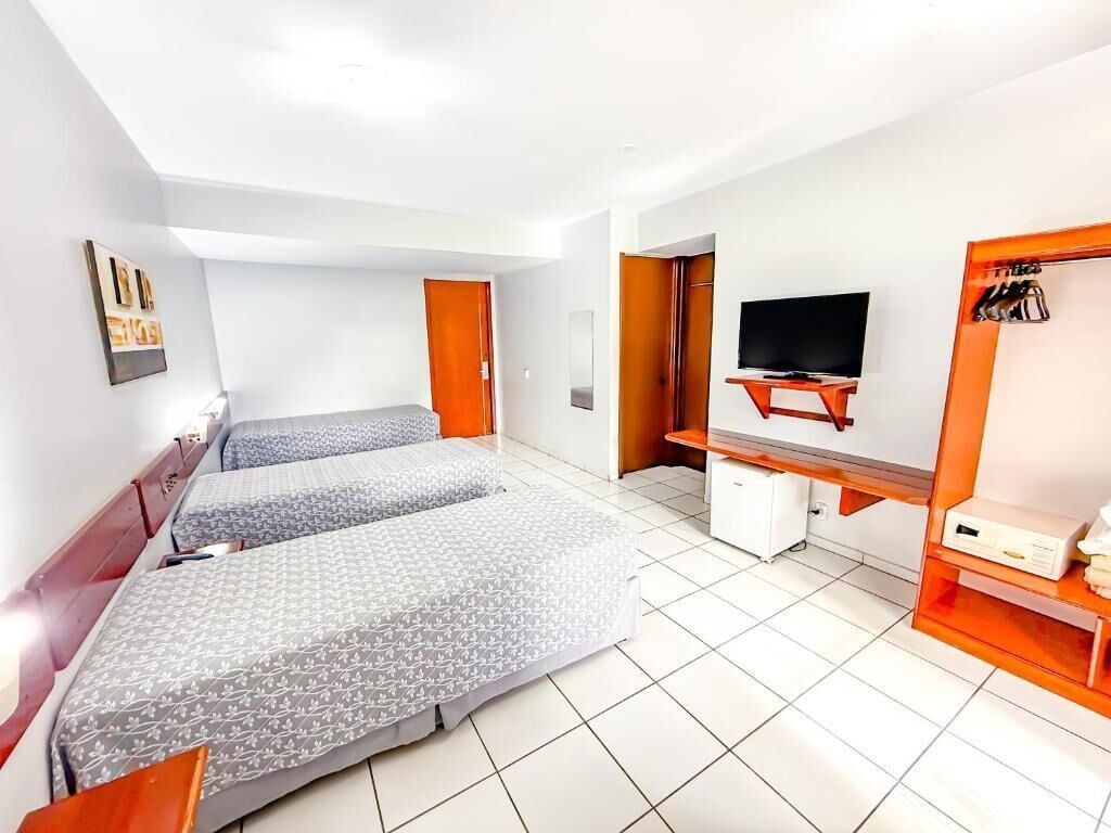 Quarto de hotel com duas camas, televisão, escrivaninha e armário.