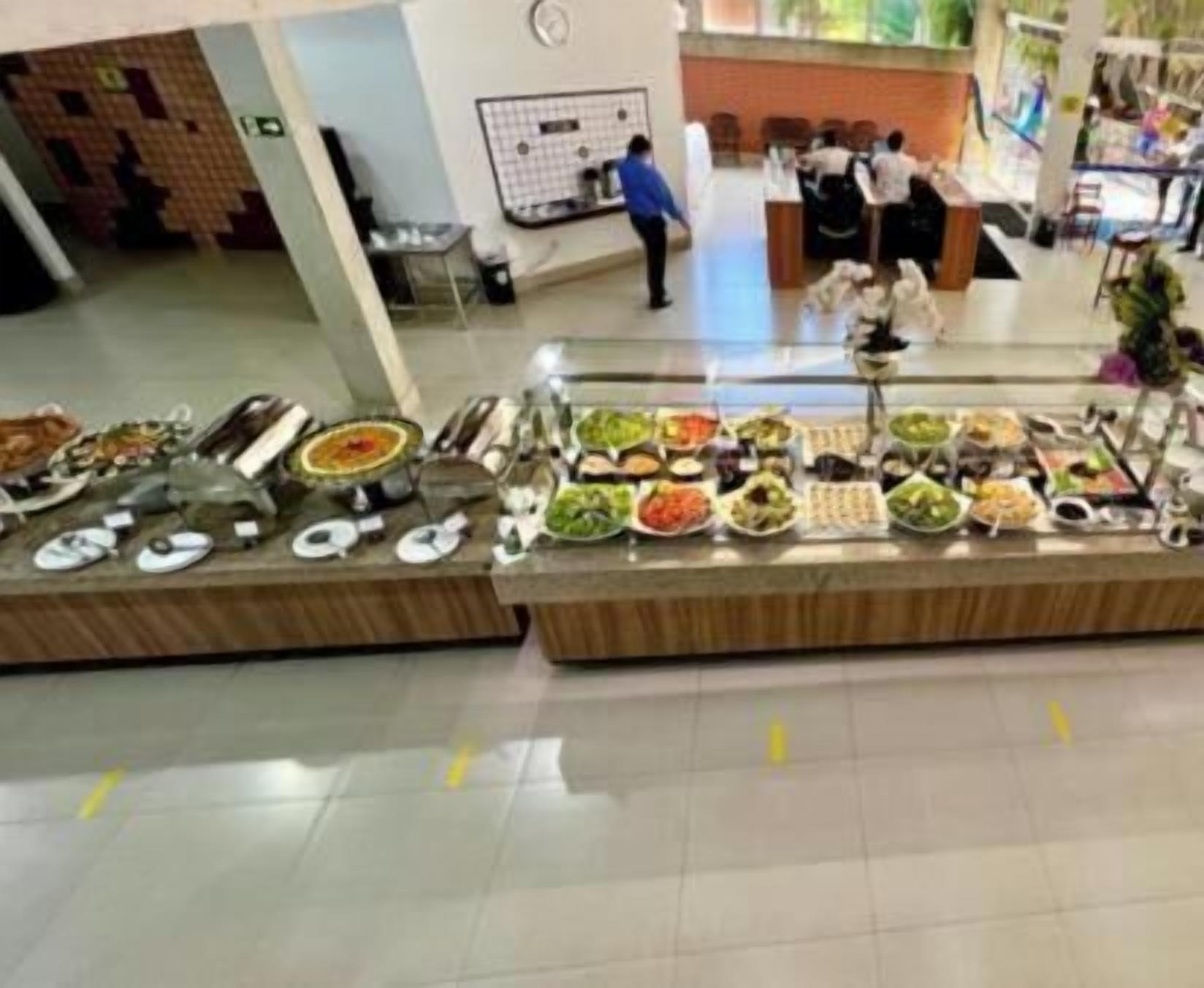 Uma área de buffet com diversos pontos de alimentação e um espaço com assentos ao fundo.