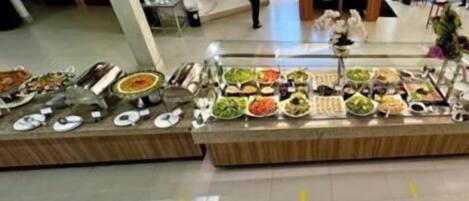 Uma área de buffet com diversos pontos de alimentação e um espaço com assentos ao fundo.
