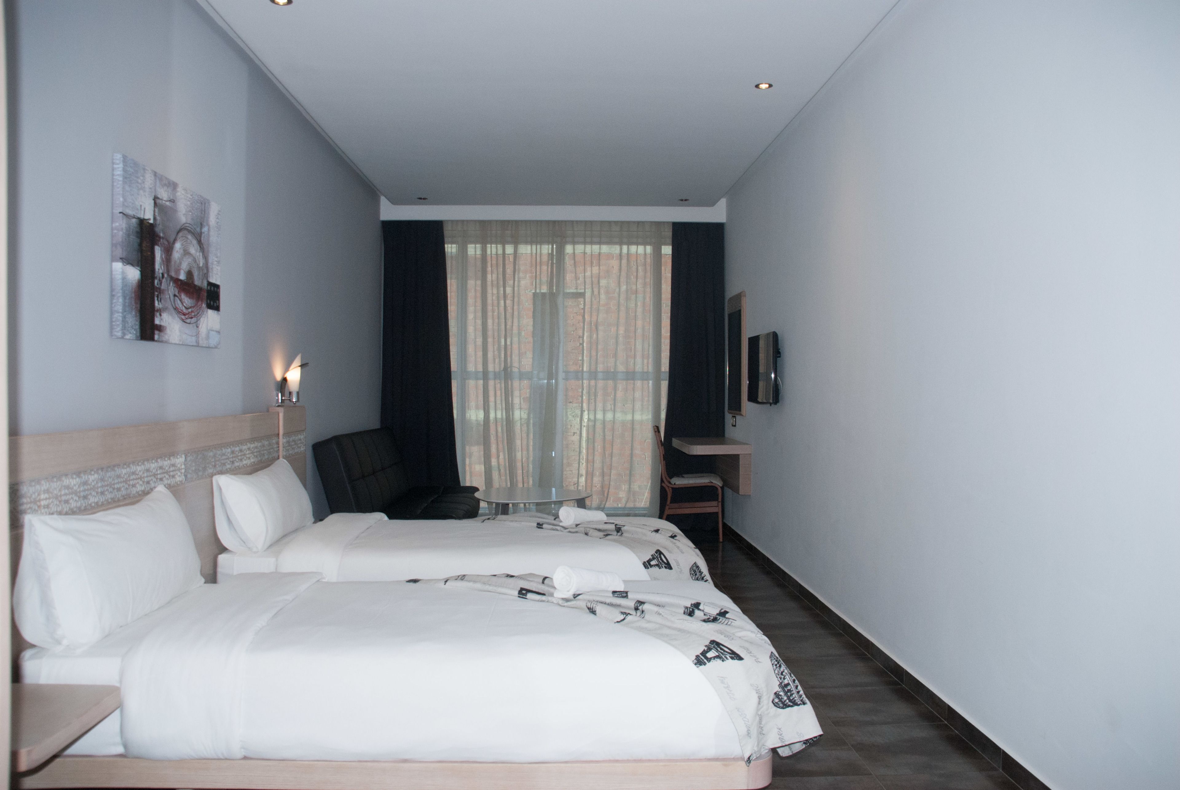 Quarto de hotel com duas camas, uma escrivaninha, uma cadeira, uma televisão e uma janela com cortinas.