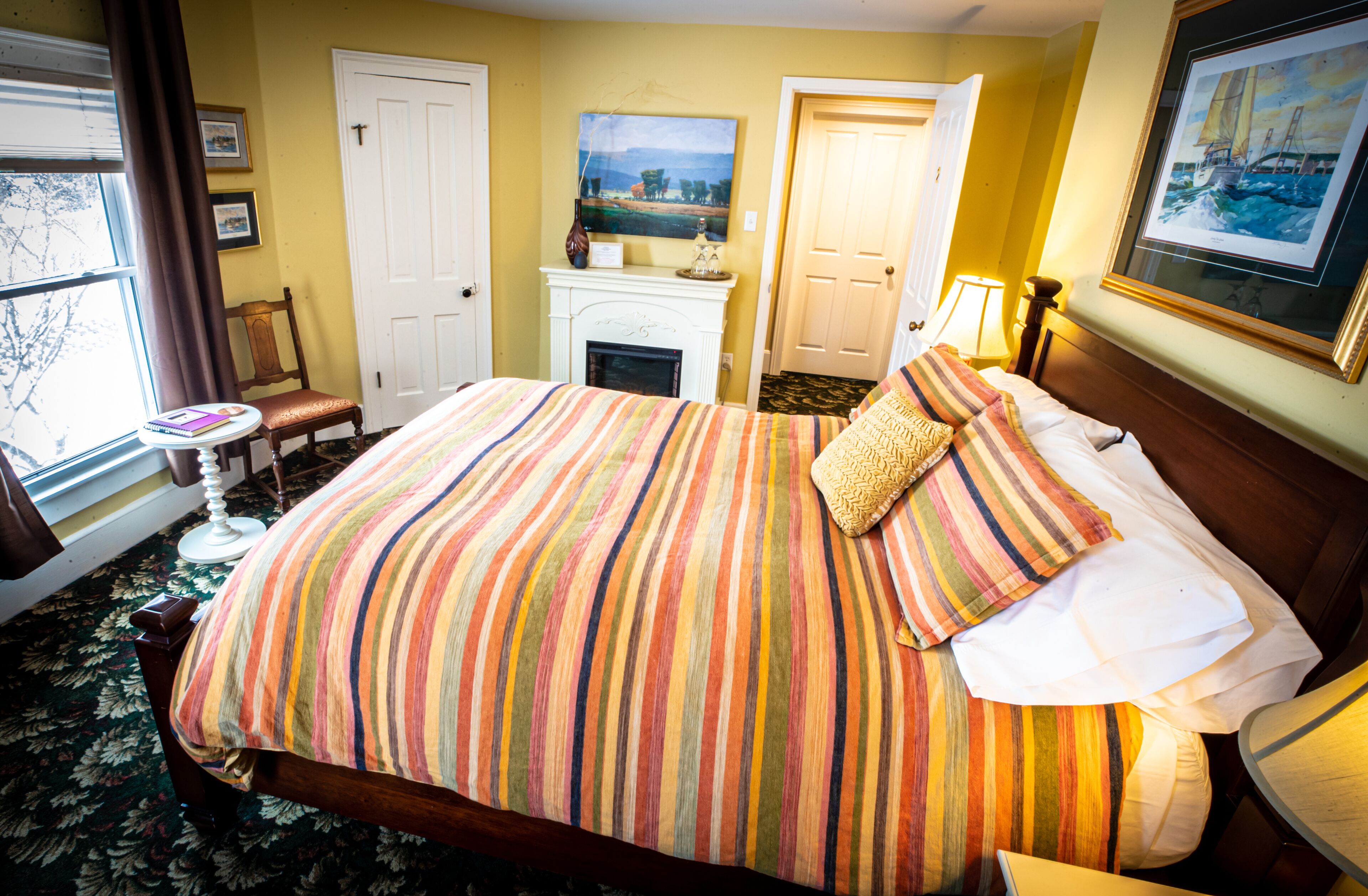 Quarto de hotel com uma cama grande, lareira, uma cadeira e janela com cortinas.