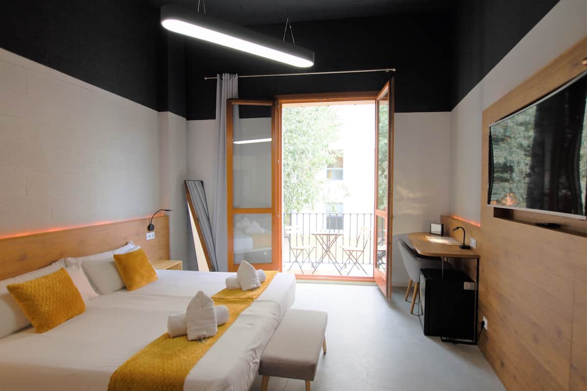 Quarto de hotel com duas camas, uma escrivaninha e vista para o exterior.