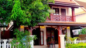 Uma casa de madeira tradicional com varanda, plantas em vasos e uma placa indicando ser uma villa.