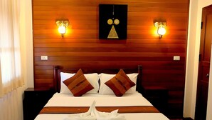 Cama bem arrumada com roupa de cama branca e almofadas castanhas, cabeceira de madeira, duas luzes fixadas na parede e um quadro emoldurado acima da cama.