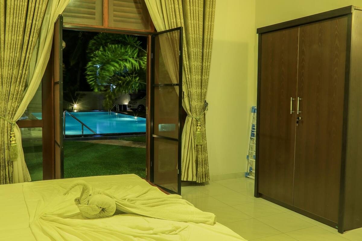 Quarto com cama, armário e vista para uma piscina ao ar livre à noite.
