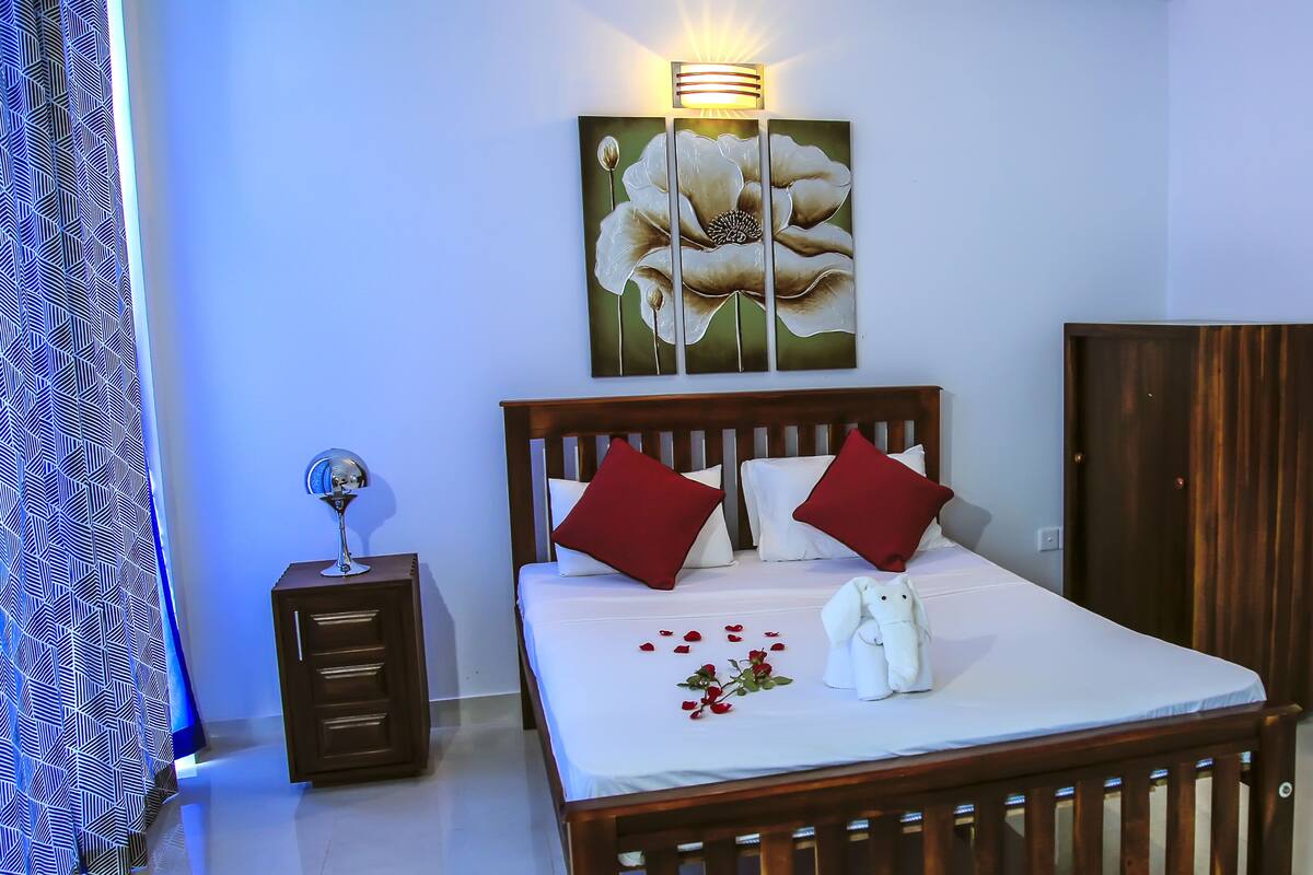 Quarto bem arrumado com cama de madeira, almofadas vermelhas e brancas, abajur e um objeto decorativo na parede acima da cama.