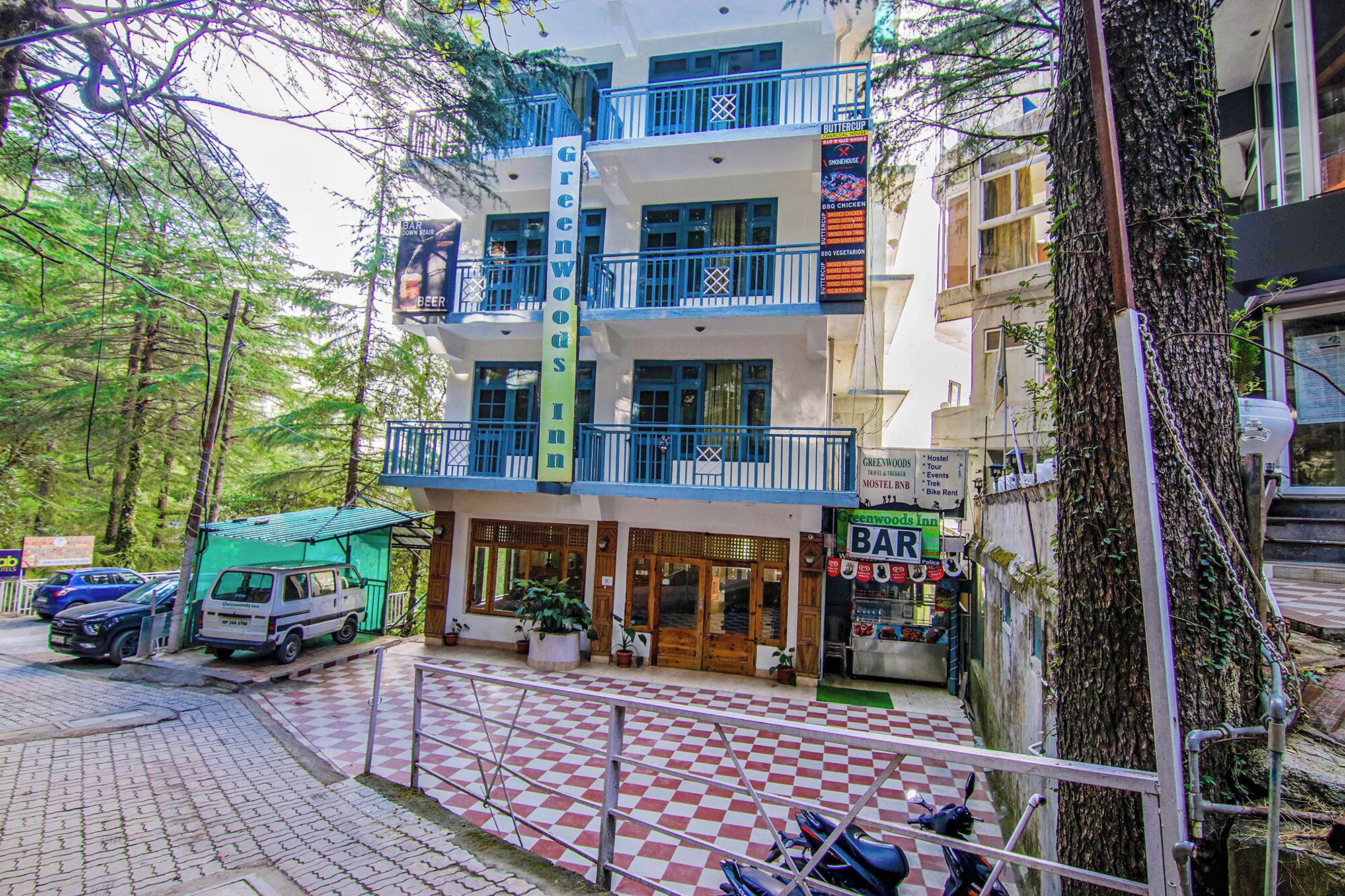 Um edifício com vários andares, fachada verde e branca, um bar e um restaurante chamado 'Greenwoods Inn'.