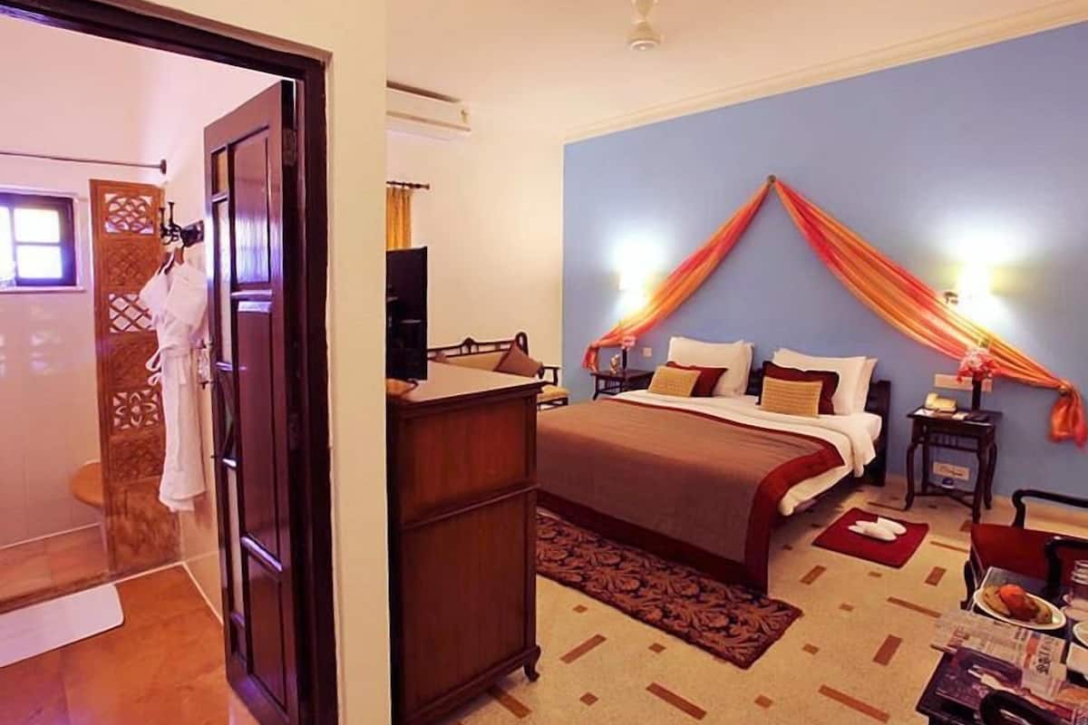Quarto de hotel com cama, escrivaninha, cadeira, mesa de cabeceira e banheiro visível por uma porta aberta.