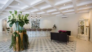 Um hall amplo com teto alto, um arranjo de plantas central, um espaço para sentar e um relógio decorativo.
