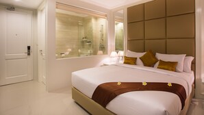 Quarto de hotel moderno com uma cama grande, chuveiro em cabine de vidro e um espelho amplo.