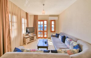 Uma sala de estar com sofá, mesa de centro, televisão e janela com cortinas.