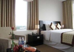 Quarto de hotel com cama, mesa de cabeceira, abajur e vista para o exterior.