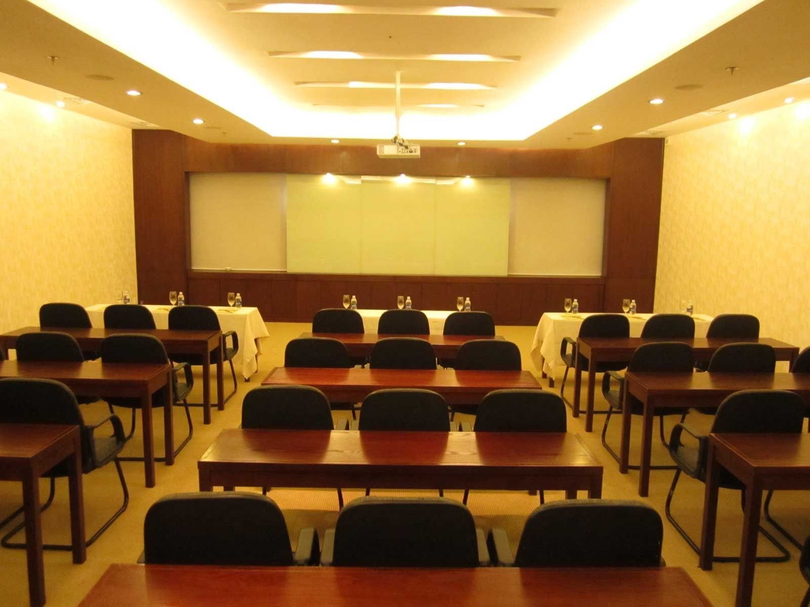 Uma sala de conferência com várias mesas e cadeiras, uma tela de projetor e um quadro branco.