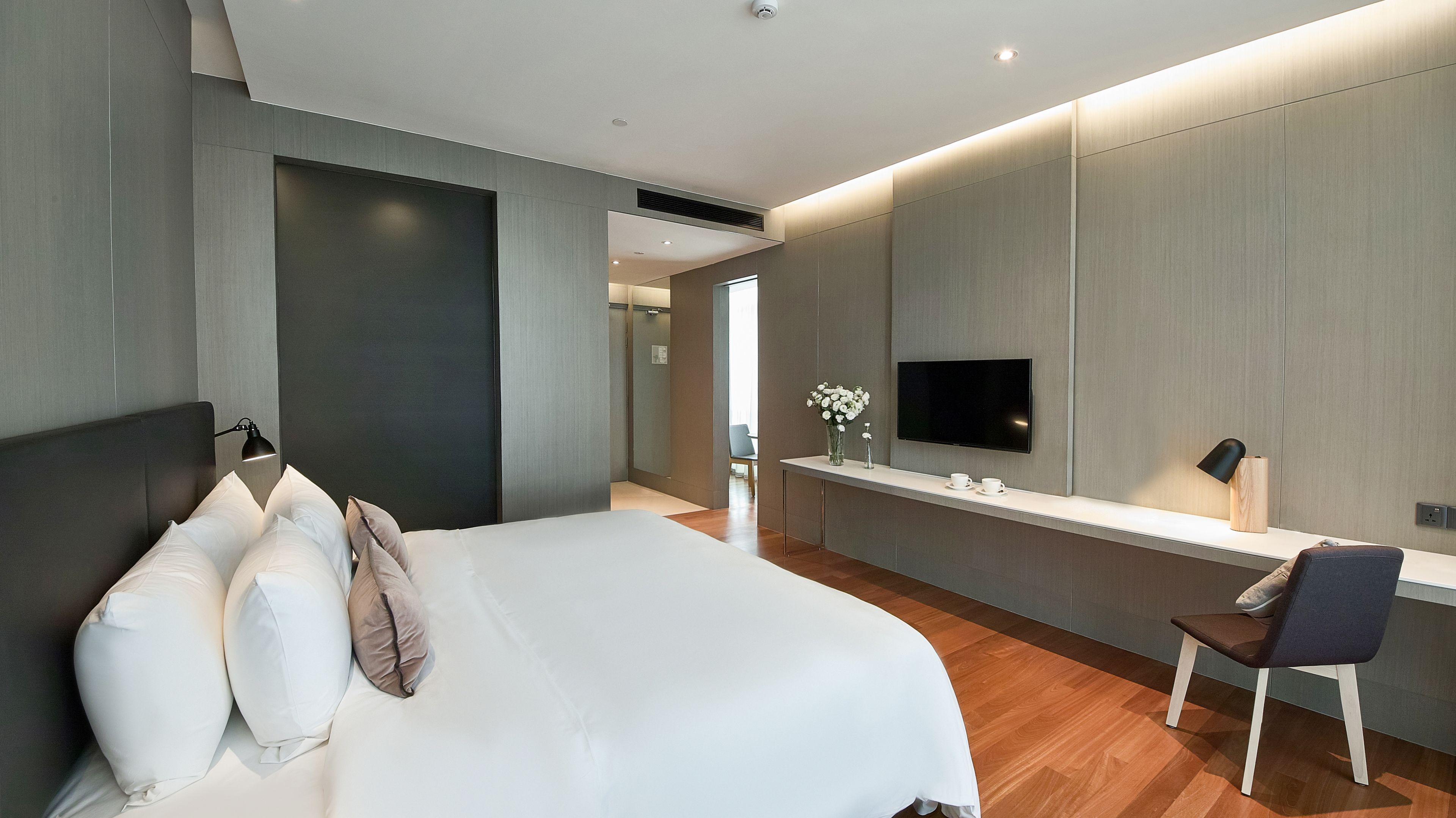 Quarto de hotel moderno com uma cama grande, uma escrivaninha com cadeira, televisão de tela plana e um vaso com flores.
