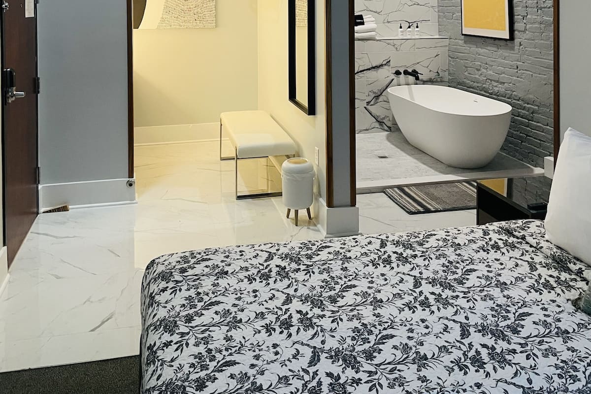 Quarto moderno com cama grande, um banco embutido, ventoinha de teto e banheiro com banheira de imersão.