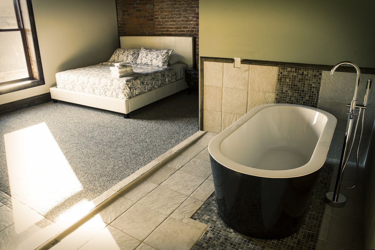 Quarto moderno com cama grande, uma banheira preta e vista da cidade pela janela.