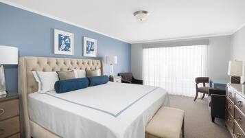 Quarto de hotel com uma cama grande, uma escrivaninha, uma cadeira e um banco.