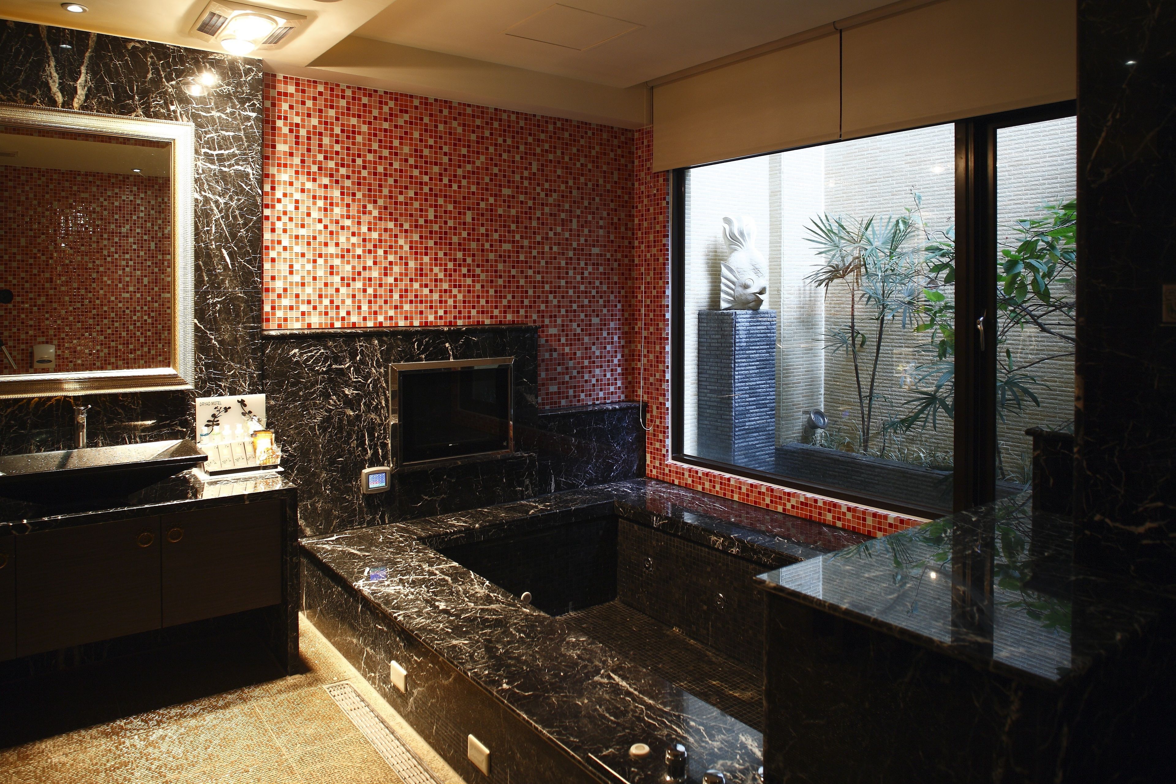 Casa de banho moderna com lavatório de mármore preto, um espelho grande e parede com mosaico vermelho.