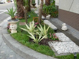 Um jardim com paisagismo, diversas plantas, um caminho e esculturas de pedra decorativas.