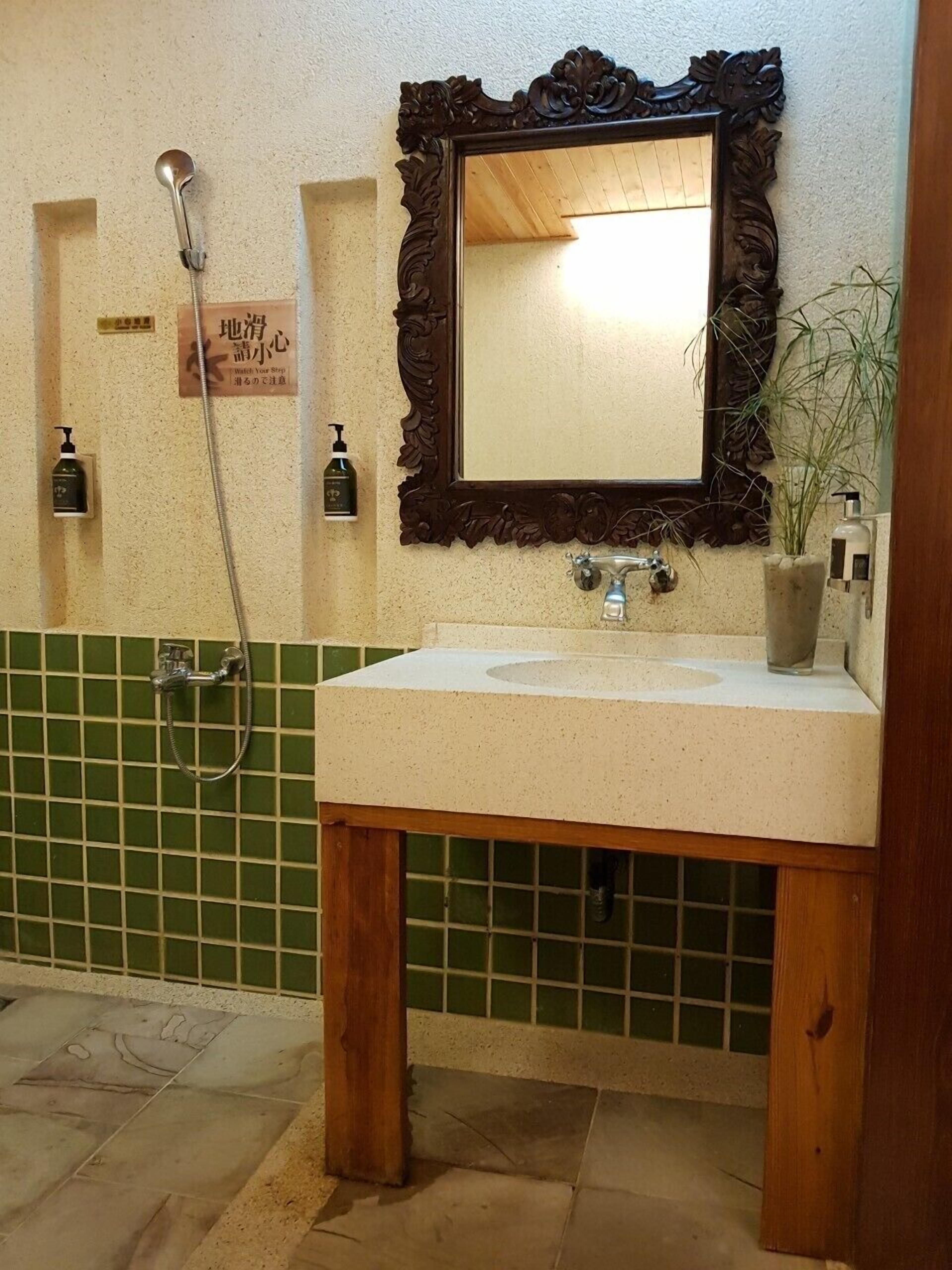 Casa de banho com lavatório, espelho, chuveiro e paredes com azulejos verdes.