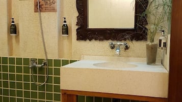 Casa de banho com lavatório, espelho, chuveiro e paredes com azulejos verdes.