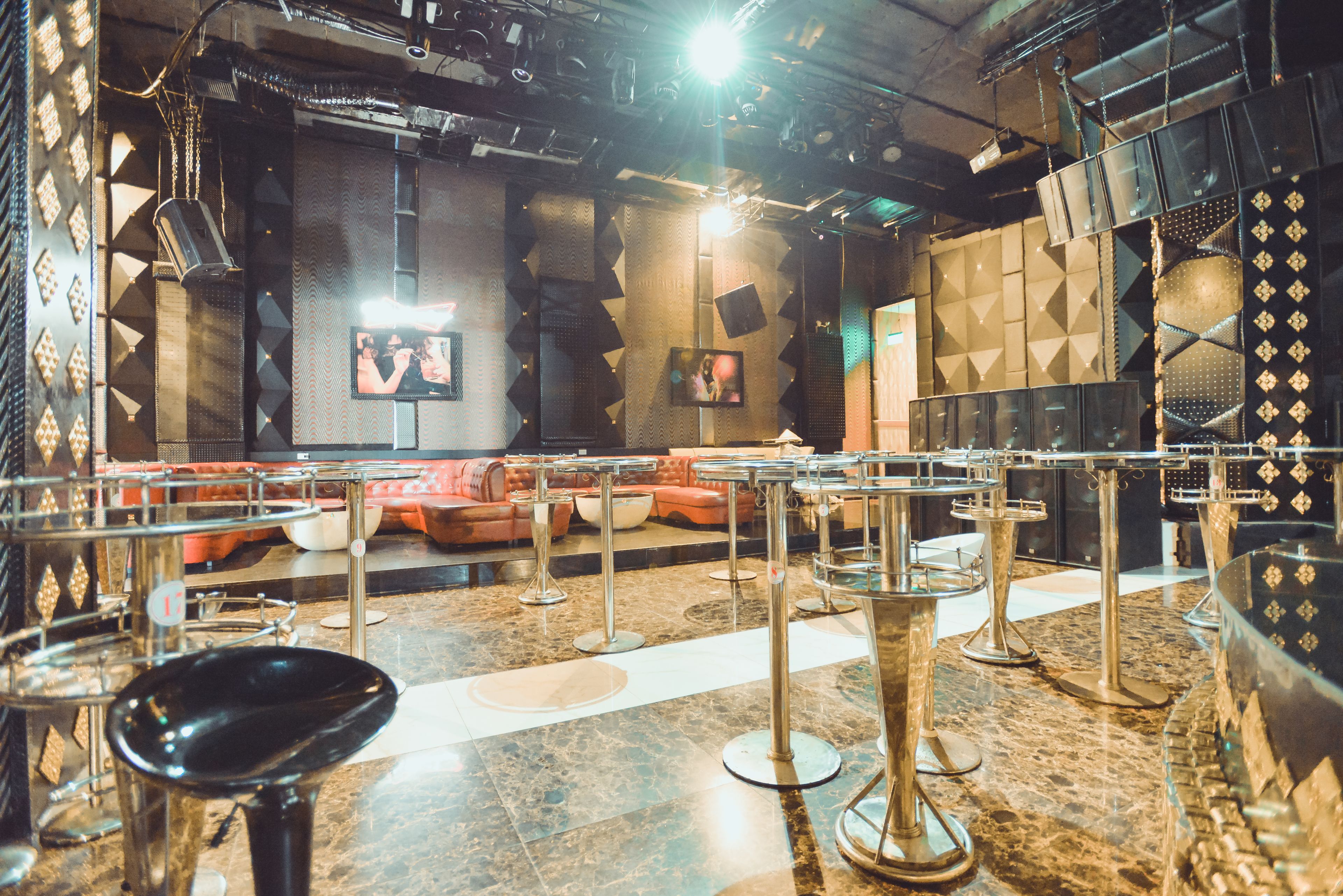 Uma área de bar com vários bancos e mesas, um espaço de estar com sofás e uma televisão na parede.