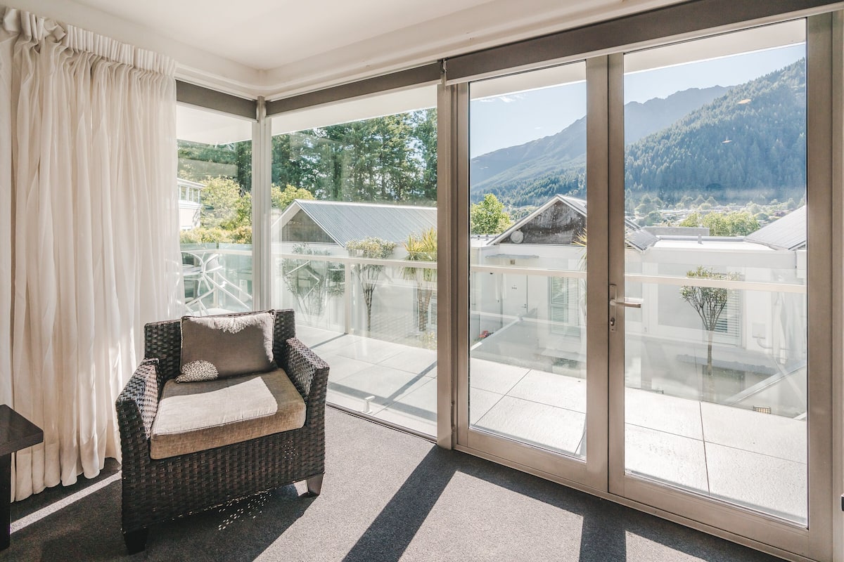 Uma varanda com sofá de vime, porta de vidro e vista para casas e montanhas.