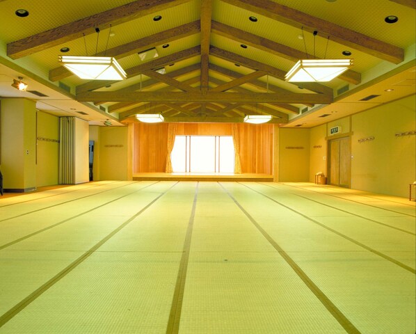 Um espaço com tatames, vigas de madeira, uma janela grande com cortinas e um balcão de recepção.
