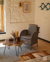 Um quarto acolhedor com uma cadeira de vime, uma mesa redonda pequena com um vaso e quadros nas paredes.