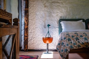 Quarto com parede de pedra rústica, estrutura de cama de madeira e luminária de chão pendente.