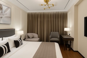 Quarto de hotel com cama, duas cadeiras, escrivaninha e ventilador de teto.