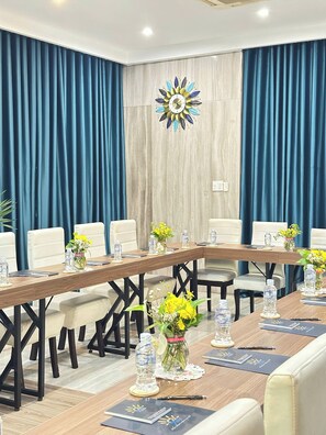 Uma sala de conferência com uma mesa comprida, cadeiras brancas e centros de mesa florais.