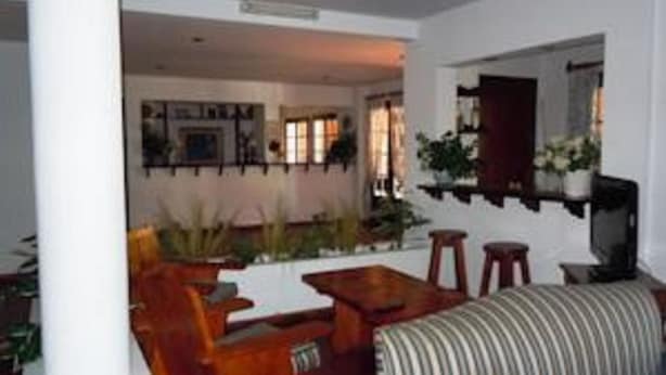 Uma sala de estar com um sofá, uma mesa de centro e uma televisão. Há uma planta e uma estante com objetos decorativos.