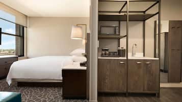 Quarto de hotel com cama, secretária com abajur, armário, micro-ondas e pia.