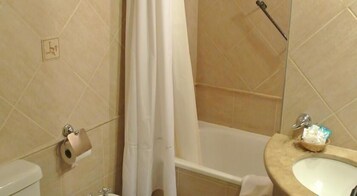 Um banheiro com azulejos bege, vaso sanitário, pia com espelho e área de chuveiro.