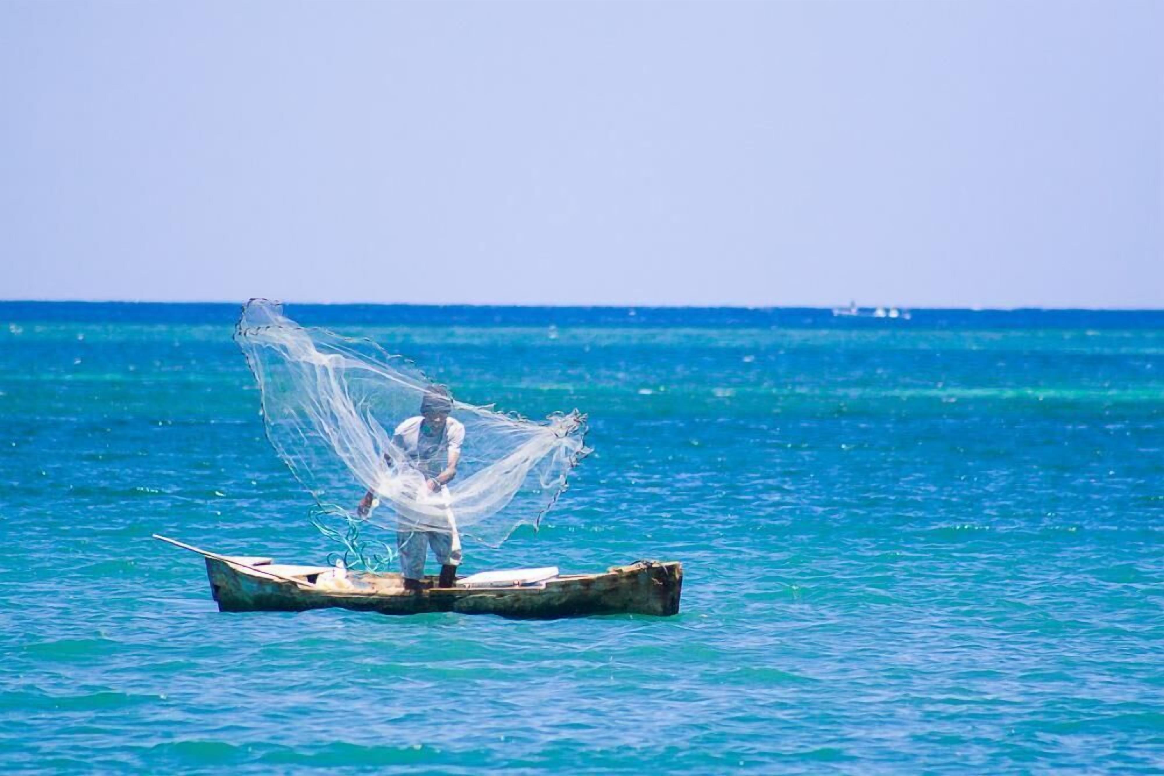 Uma pessoa em um barco pequeno na água, lançando uma rede de pesca.