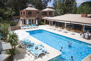 Uma área de piscina com espreguiçadeiras, piscina e um edifício com janelas amplas e varanda.