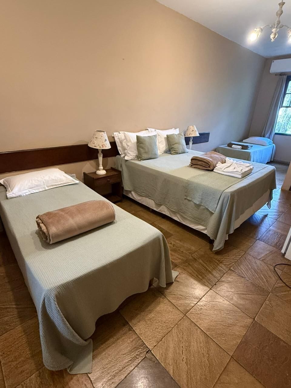 Quarto de hotel com duas camas, uma mesa de cabeceira com abajur e uma janela com cortinas.