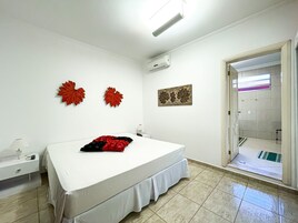 Quarto com cama, mesa de cabeceira, luminária e ar-condicionado fixado na parede.