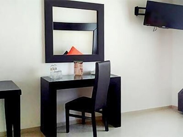 Uma pequena mesa escura com uma cadeira, um espelho e uma televisão fixada na parede.