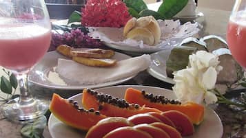 Uma mesa com diversos pratos, incluindo mamão fatiado, uma bebida vermelha e um prato com arranjo de flores.