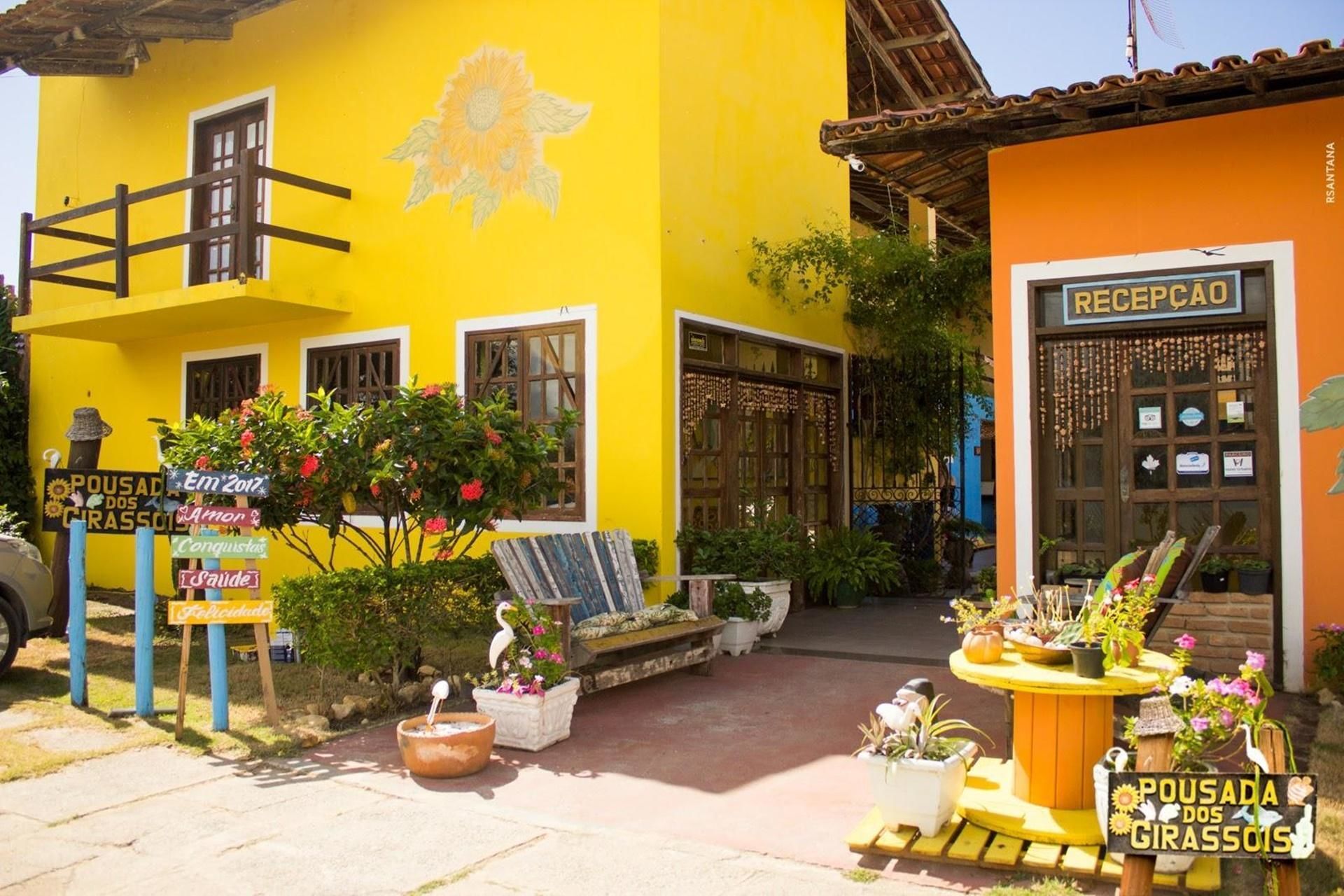 Um edifício amarelo com área de recepção e uma placa indicando "POUSADA DOS GIRAÇOIS".
