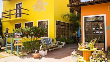 Um edifício amarelo com área de recepção e uma placa indicando "POUSADA DOS GIRAÇOIS".