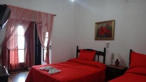 Quarto com duas camas, janela com cortinas, quadro na parede e uma mesinha com abajur.