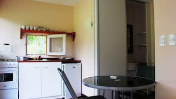 Uma cozinha compacta com armários brancos, geladeira e fogão. Há uma área de jantar com mesa de vidro e cadeiras.