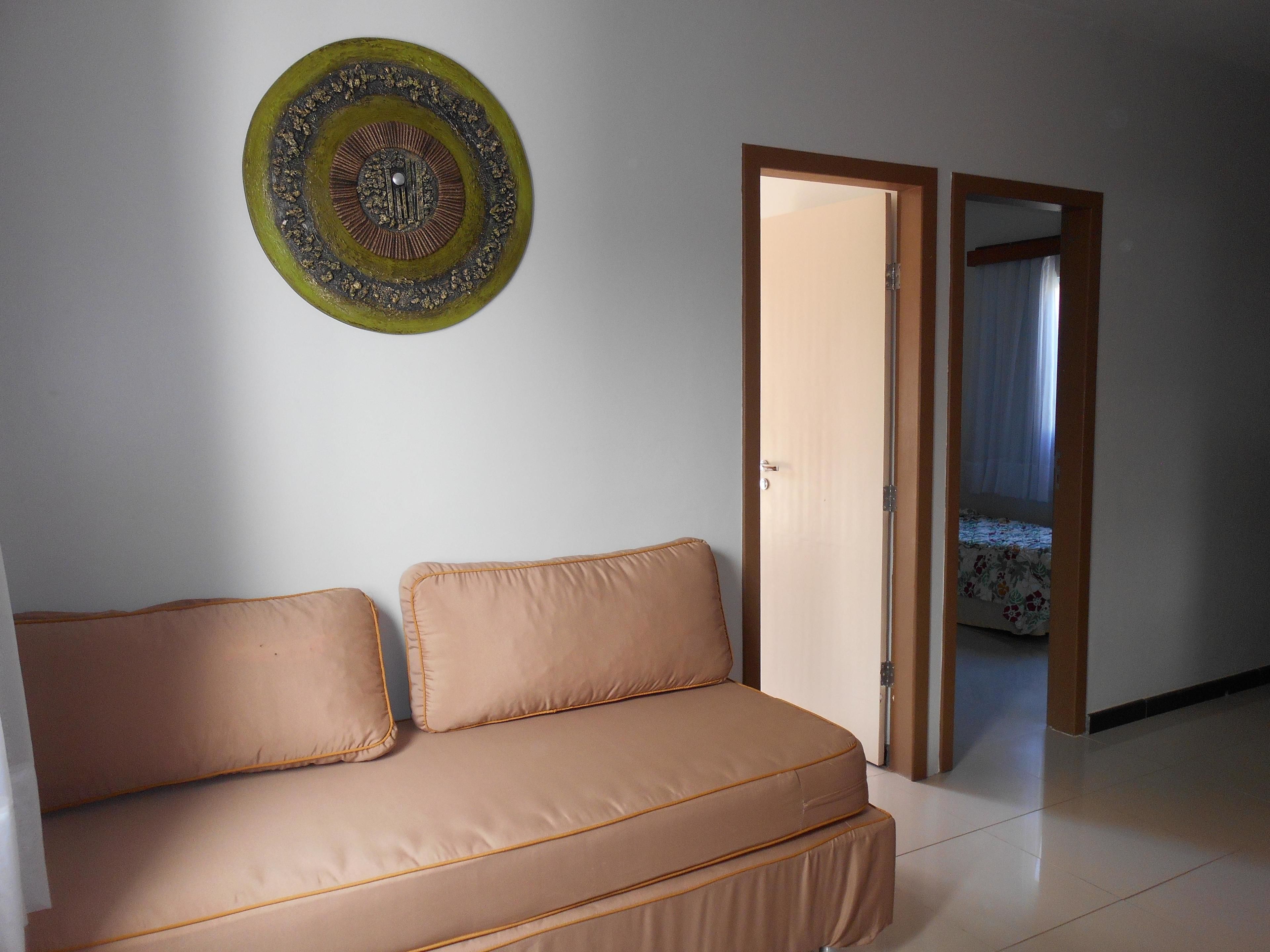 Um quarto com um sofá bege, um prato decorativo na parede e uma porta aberta para outro cômodo.