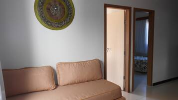 Um quarto com um sofá bege, um prato decorativo na parede e uma porta aberta para outro cômodo.