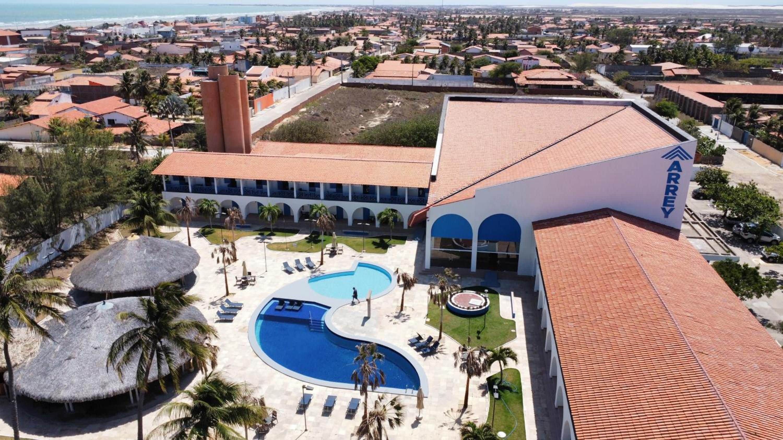 Um hotel com piscina, palmeiras e vista para a praia.