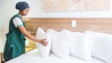Quarto de hotel com cabeceira de madeira, roupa de cama branca e um quadro na parede.